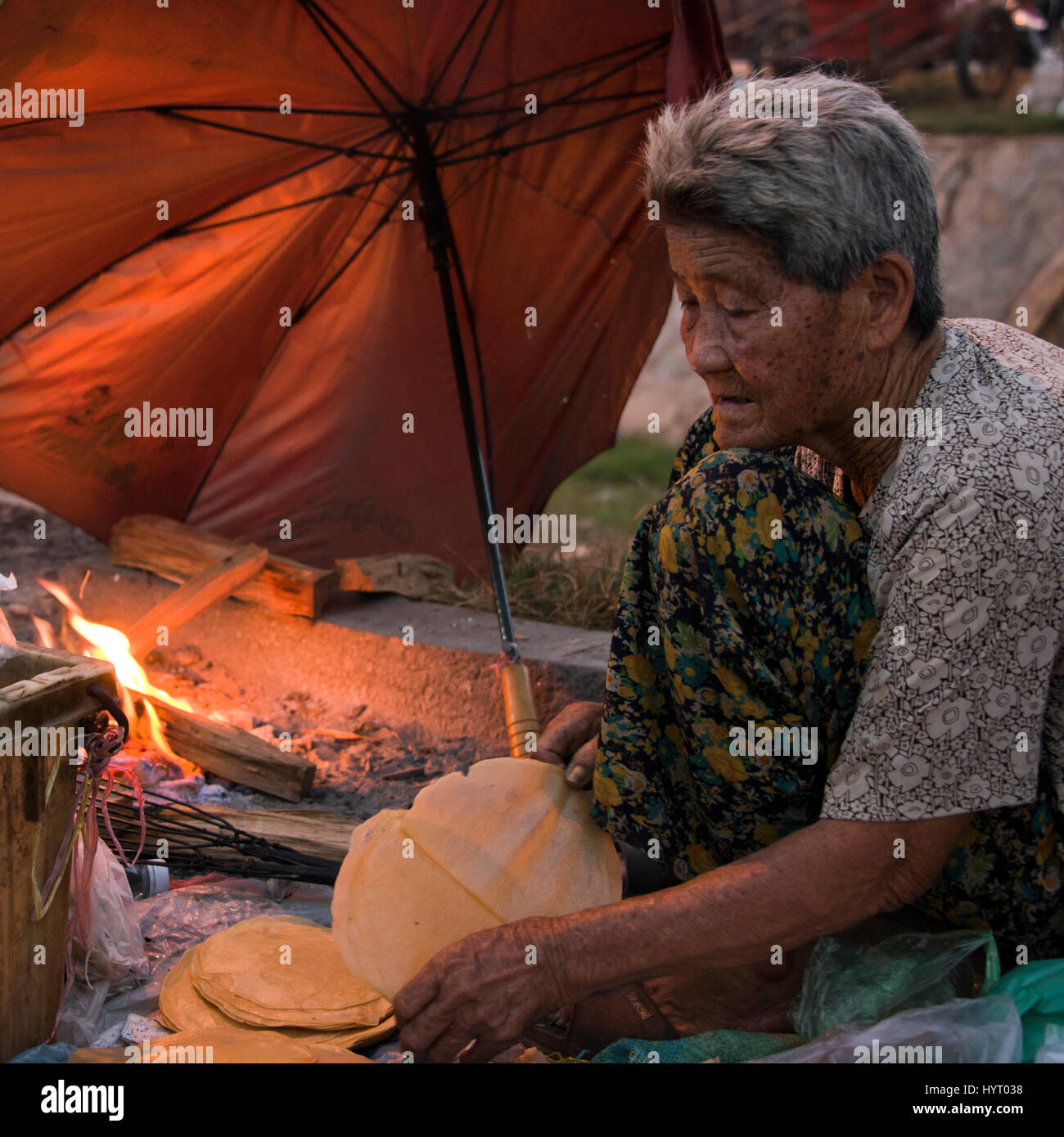 Square portrait of a poor lady making sweet rice pancakes on the street ...