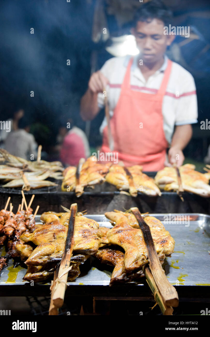 Vertical portrait of a street vendor BBQ'ing meat skewers and ...