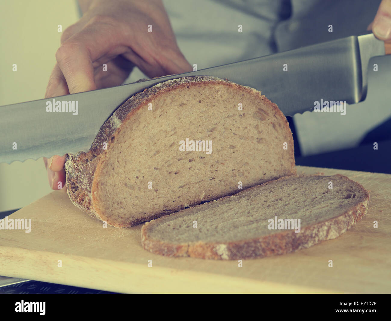 Young man is cutting bread in a modern kitchen, close up shot, natural ...