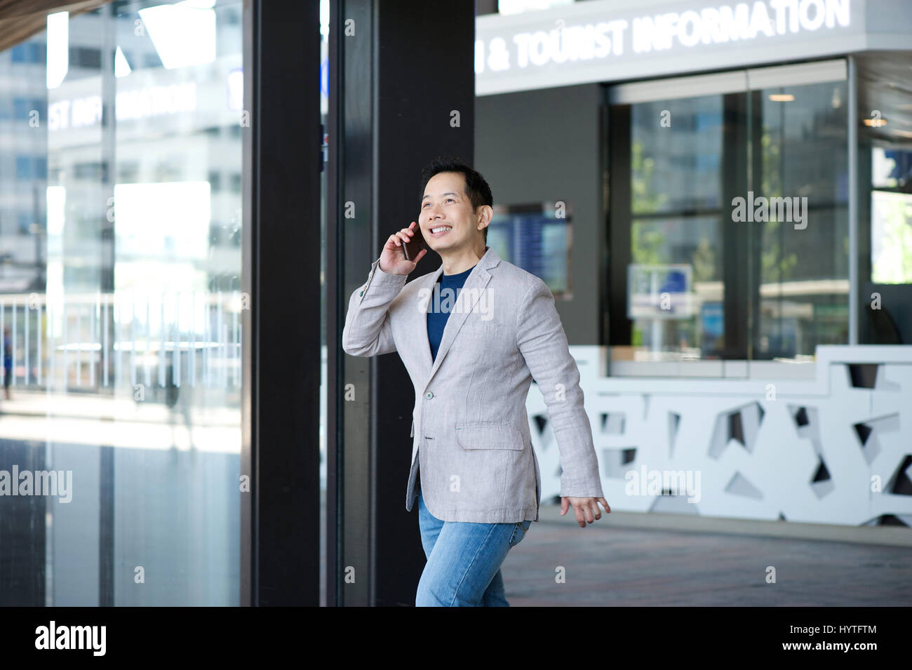 Portrait of a smiling asian man exiting building with mobile phone ...