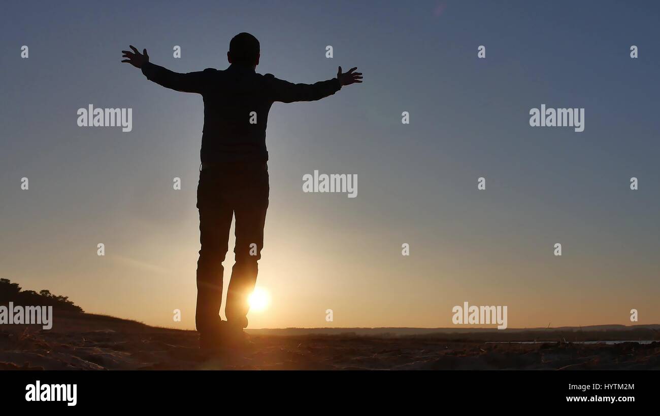 freedom. Man stands on a cliff sunset silhouette hand in the sides ...