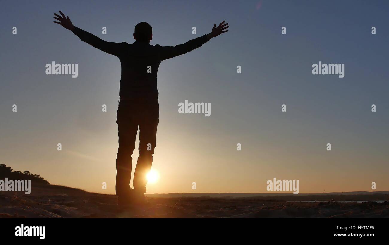 freedom. Man stands on a cliff sunset silhouette hand in the sides ...
