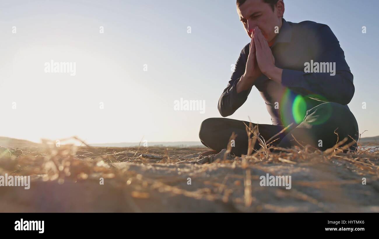 religion. Man praying sitting on the ground at sunset sun silhouette ...