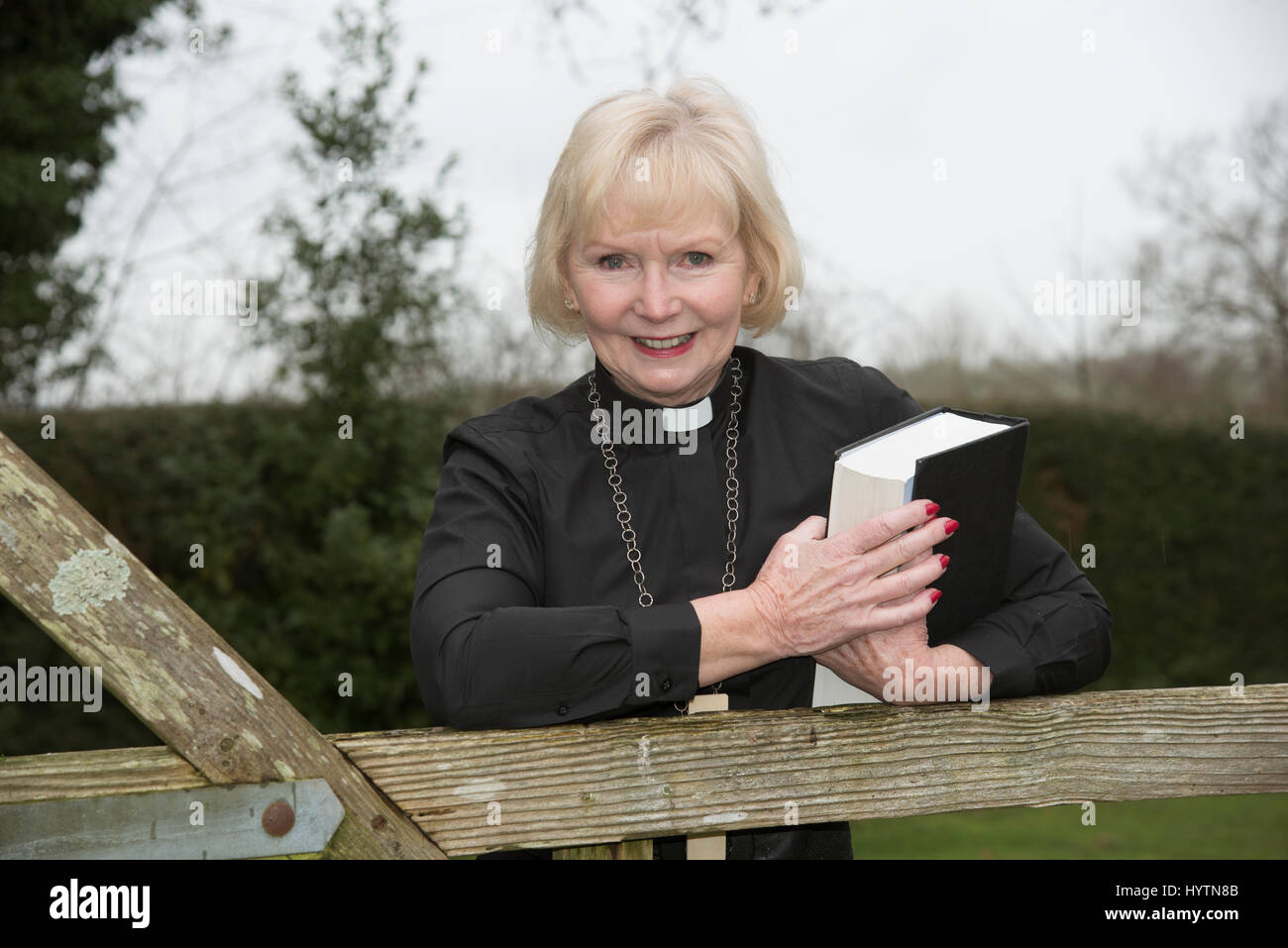 Elderly woman vicar leaning on a garden gate Stock Photo - Alamy