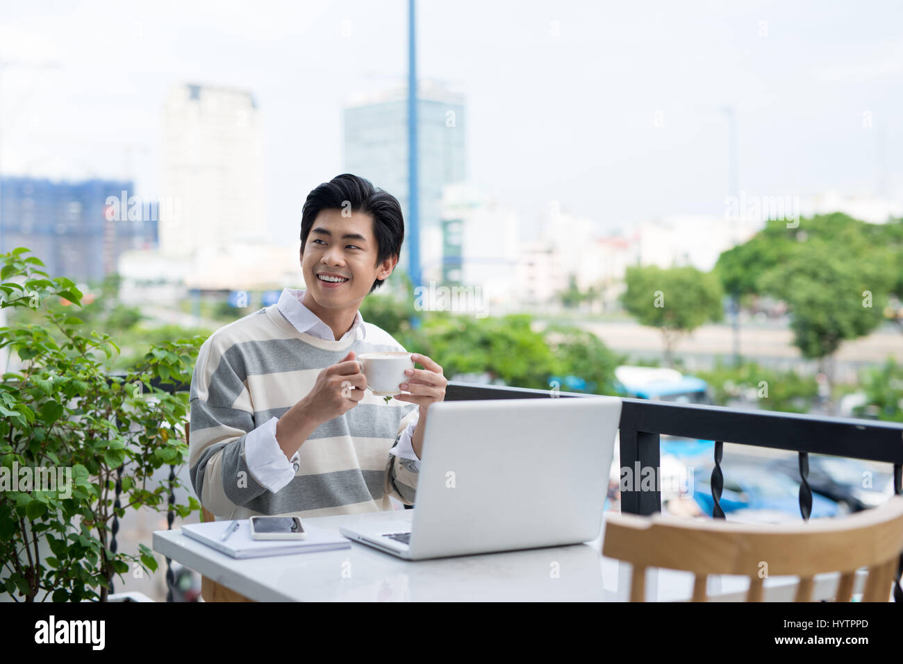 Handsome asian young man working on laptop and smiling while enjoying ...