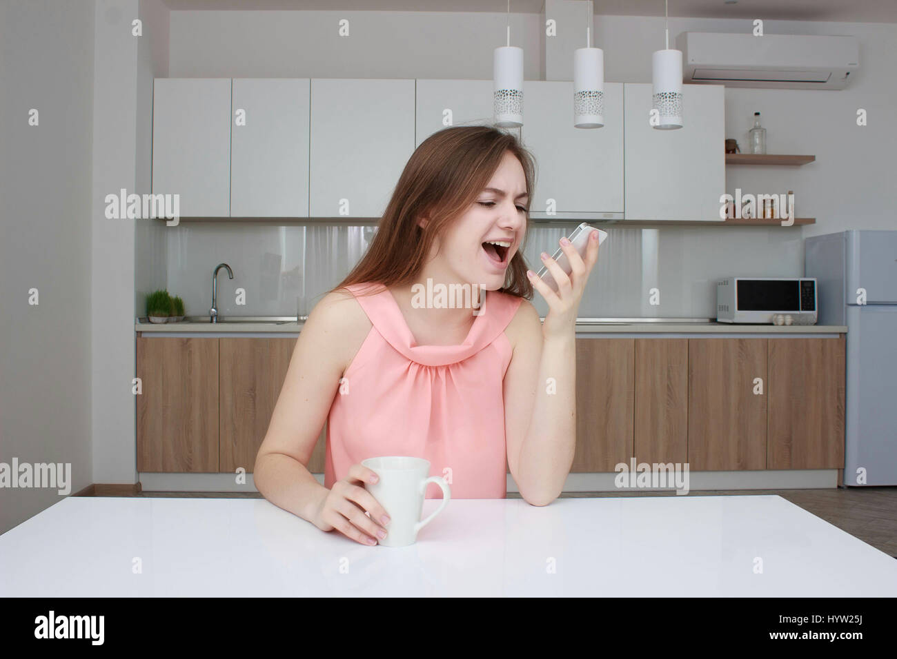 angry female With cup of tea or coffee sitting table in kitchen screams ...