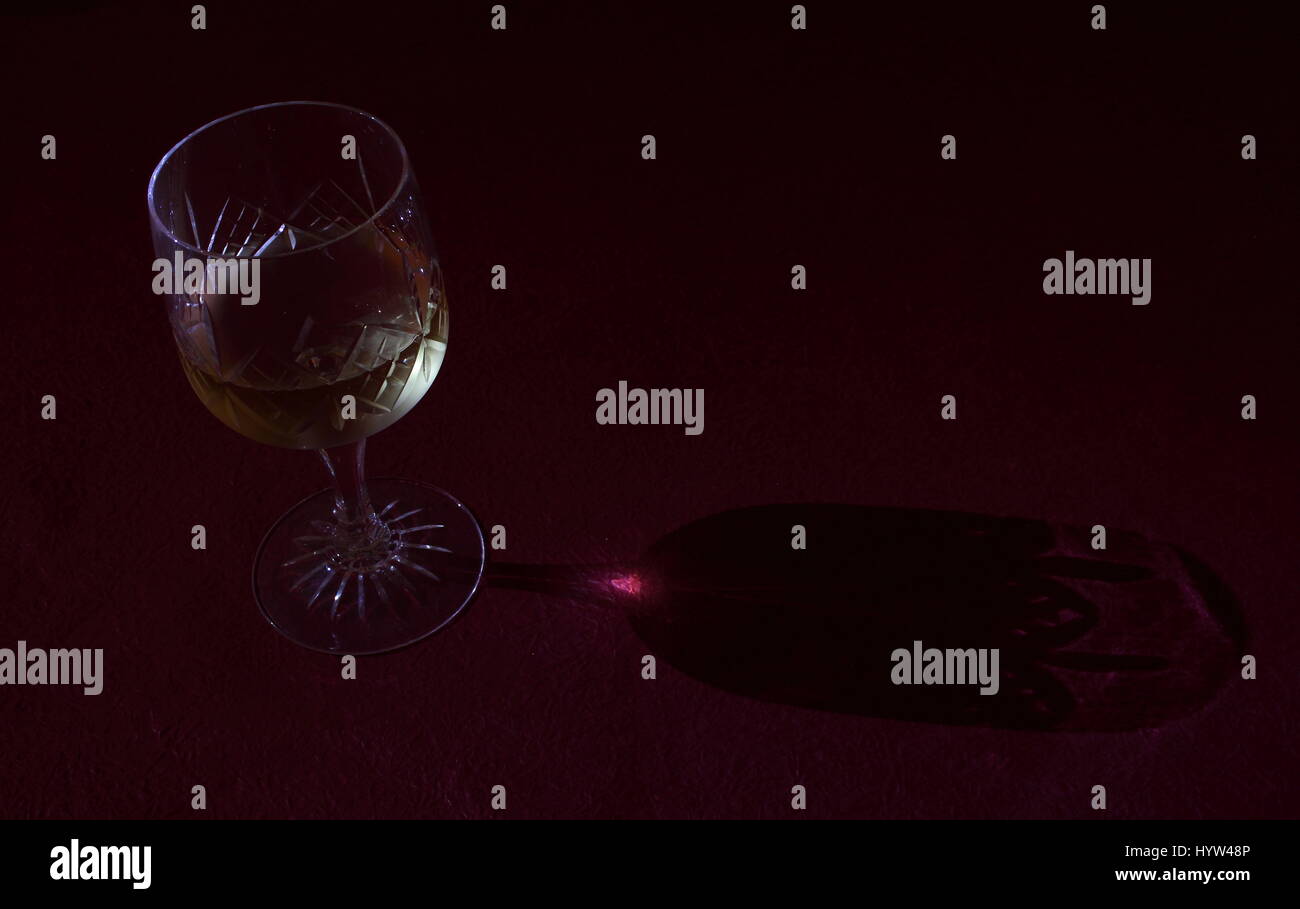 Light reflects through a glass of white wine on a deep red background ...