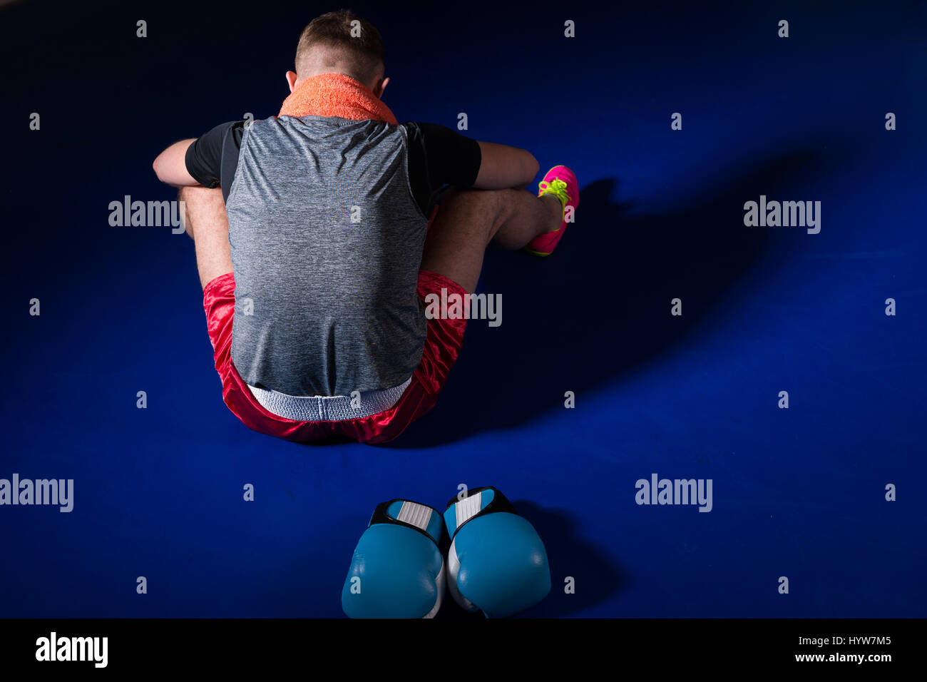 Young athletic male boxer sitting backwards near lying boxing gloves in ...