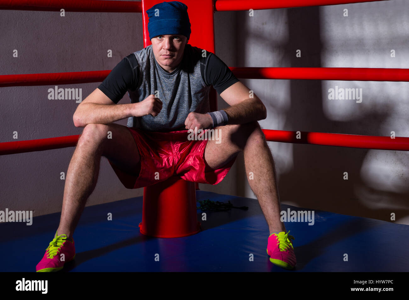 Athletic male boxer sitting near red corner of a regular boxing ring ...