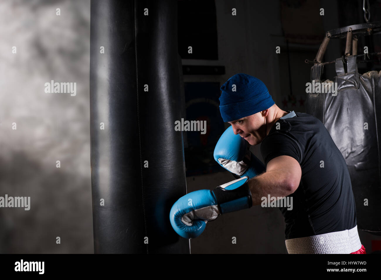 Young man in a hat and boxing gloves training with boxing punching bag ...