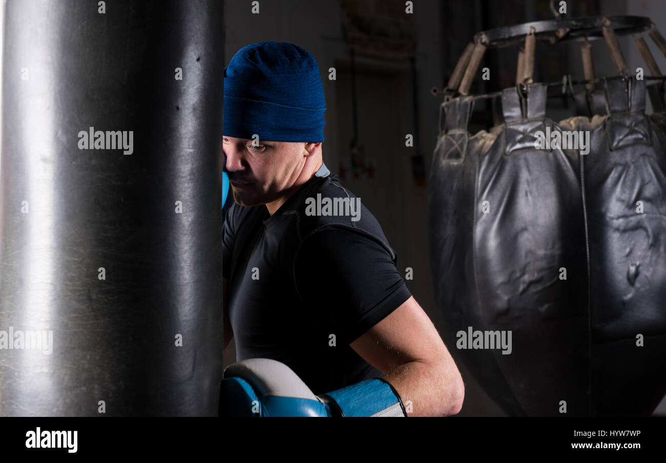 Male boxer with stern look in a hat and boxing gloves training with ...