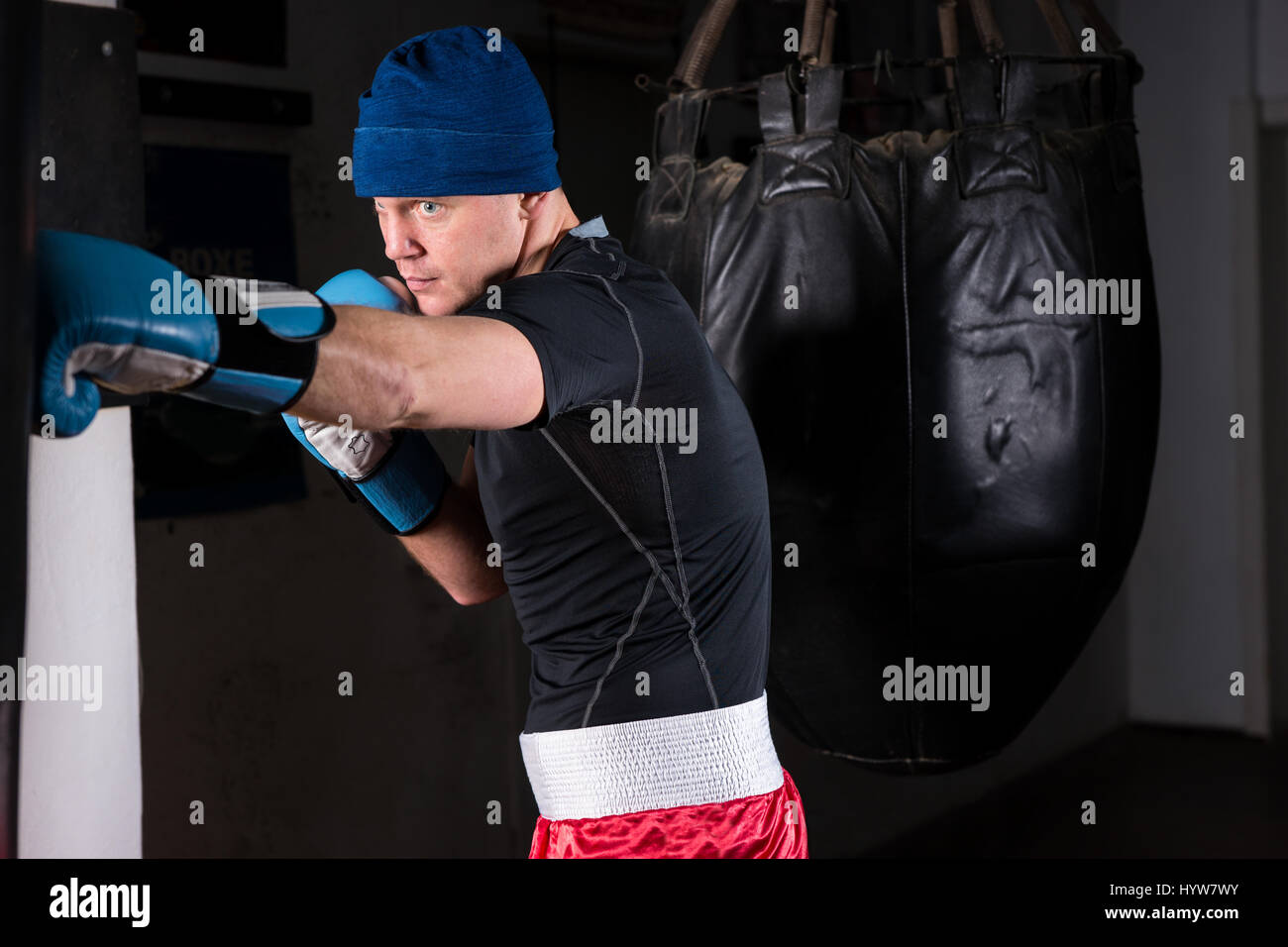 Male athletic boxer with stern look in a hat and boxing gloves training ...