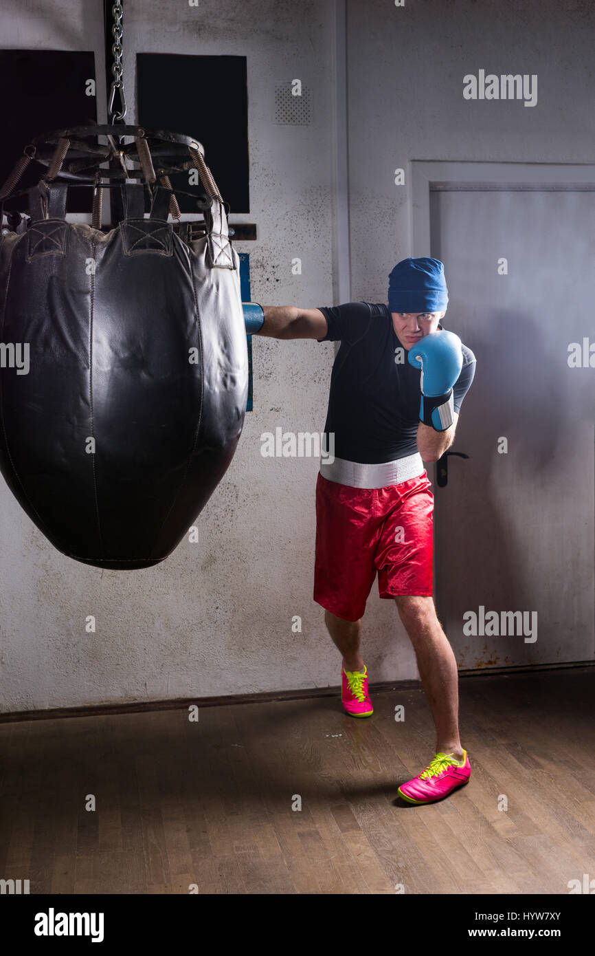 Young sporty boxer with stern look in a hat and boxing gloves training ...
