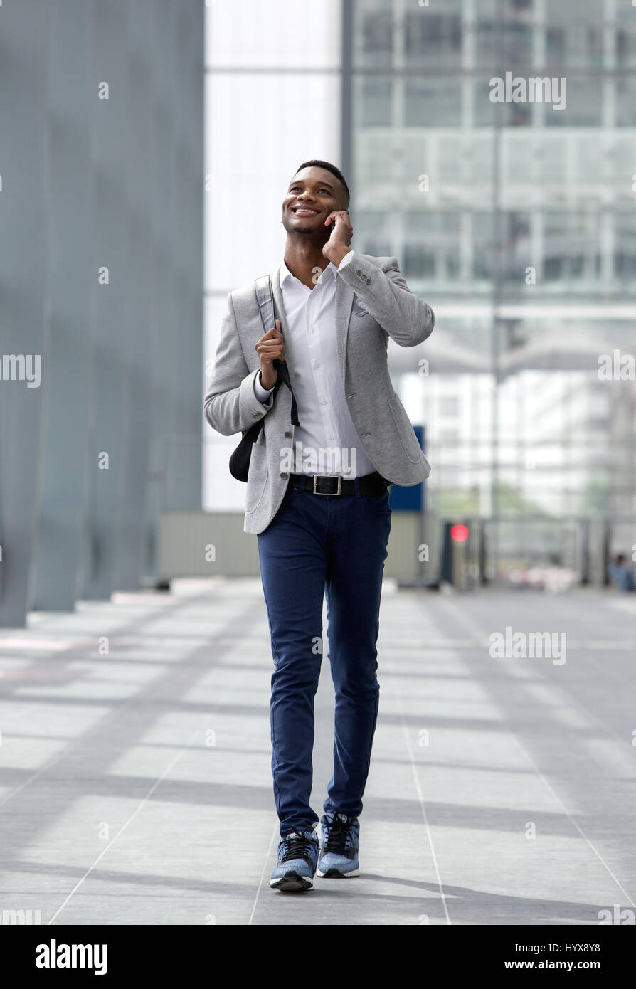 Full length portrait of a cool guy walking and talking with cellphone ...