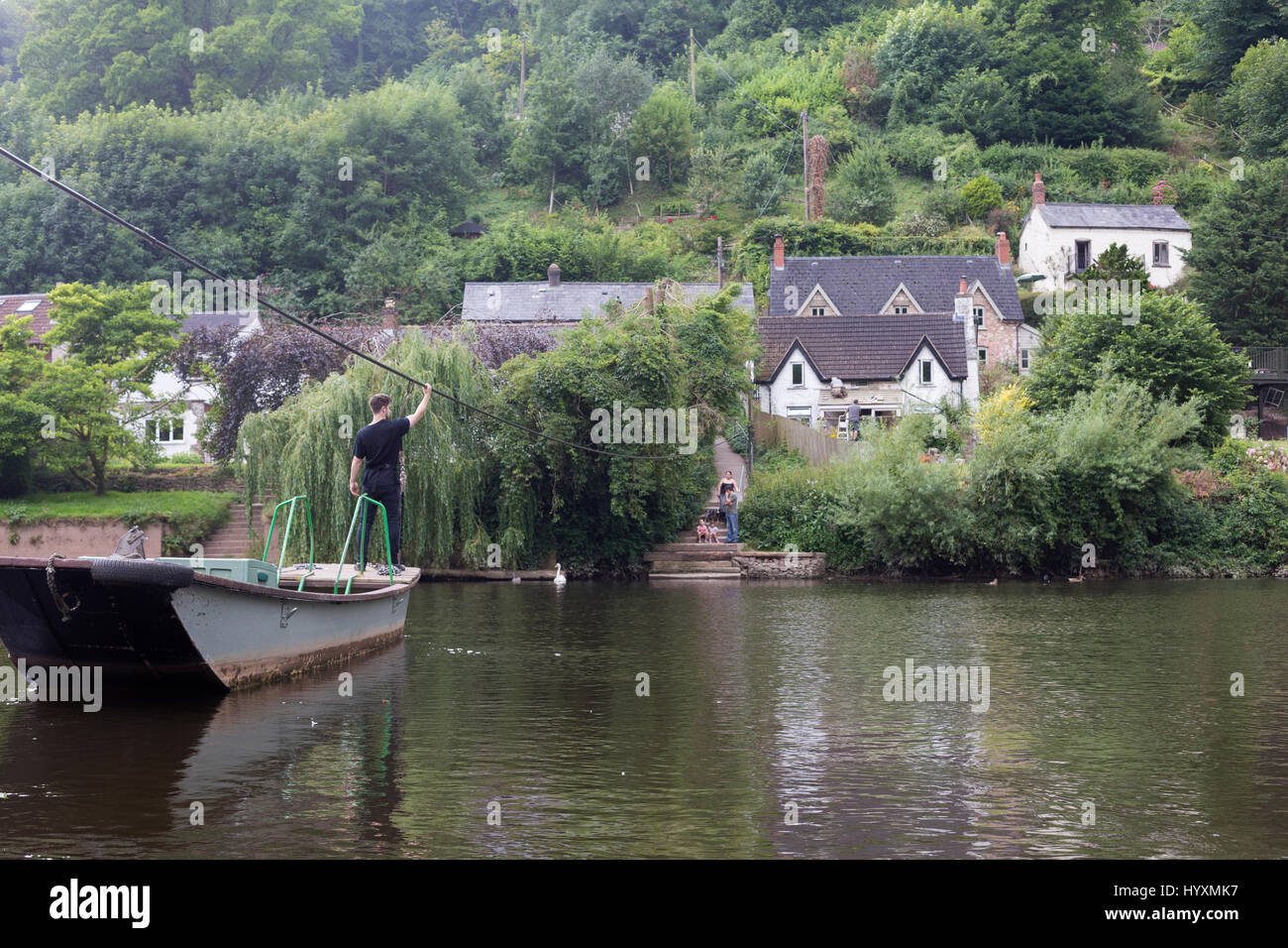 man on ferry pulling rope to reach other side with houses and trees in ...