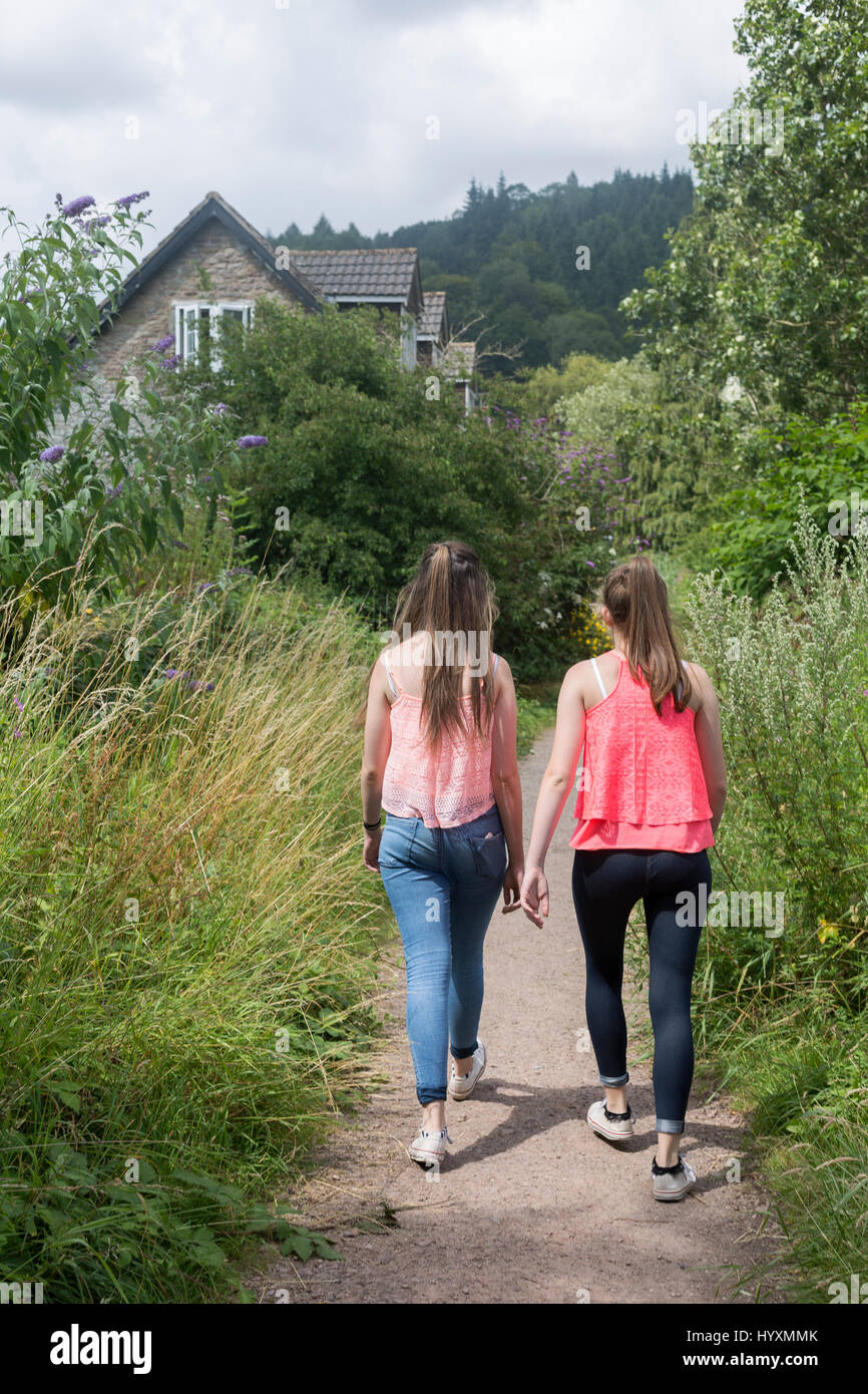 Two teenage girls walk along country lane with cottage in background ...
