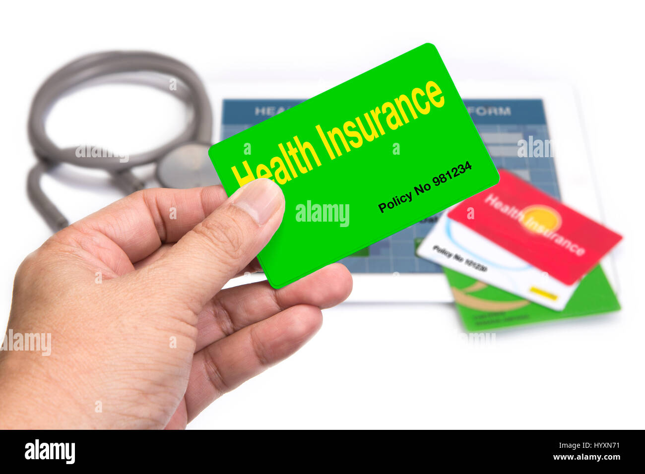 Hand holding green health insurance card in front of tablet and other ...