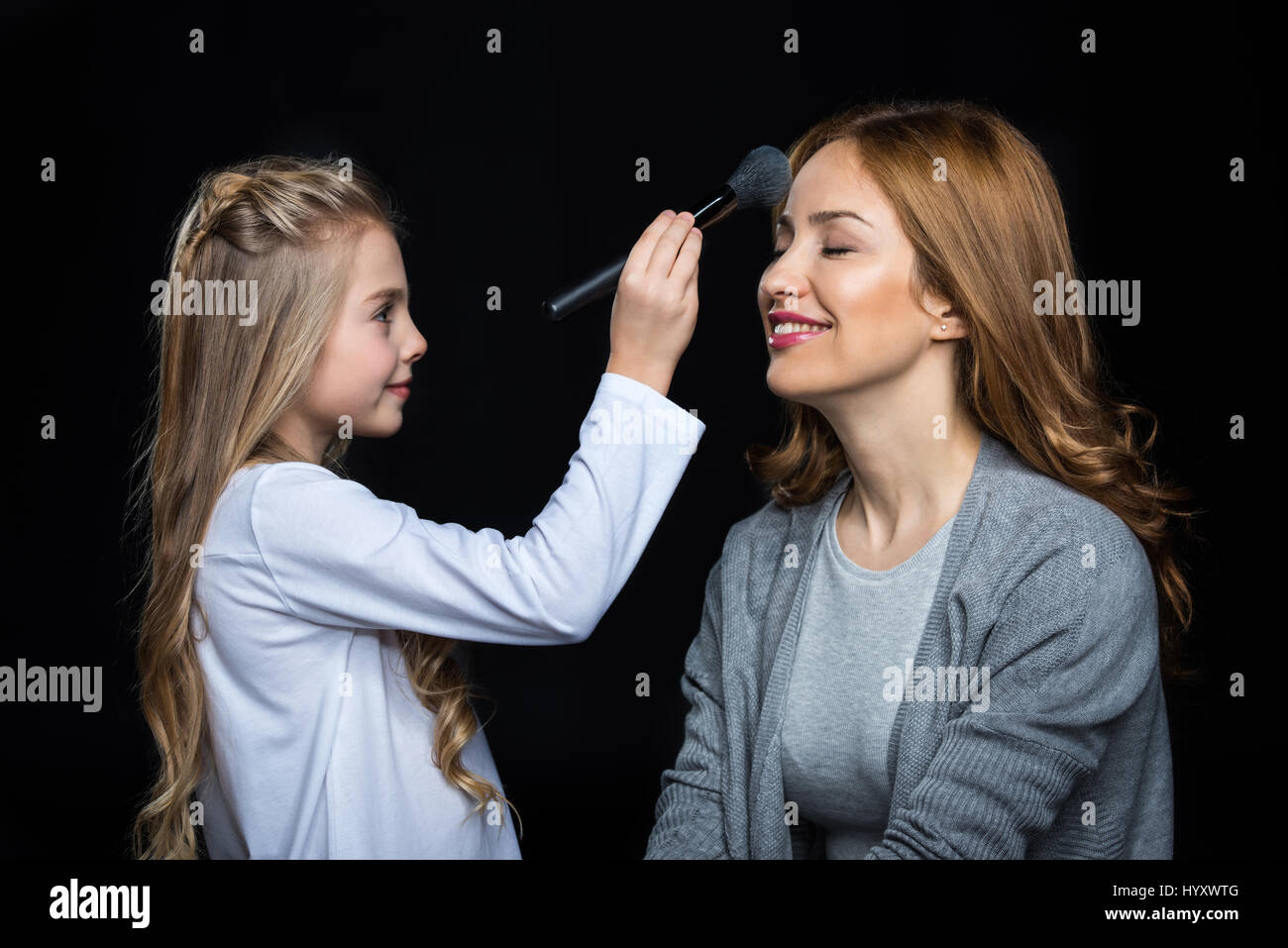 Little girl applying powder on her mother's face on black Stock Photo ...