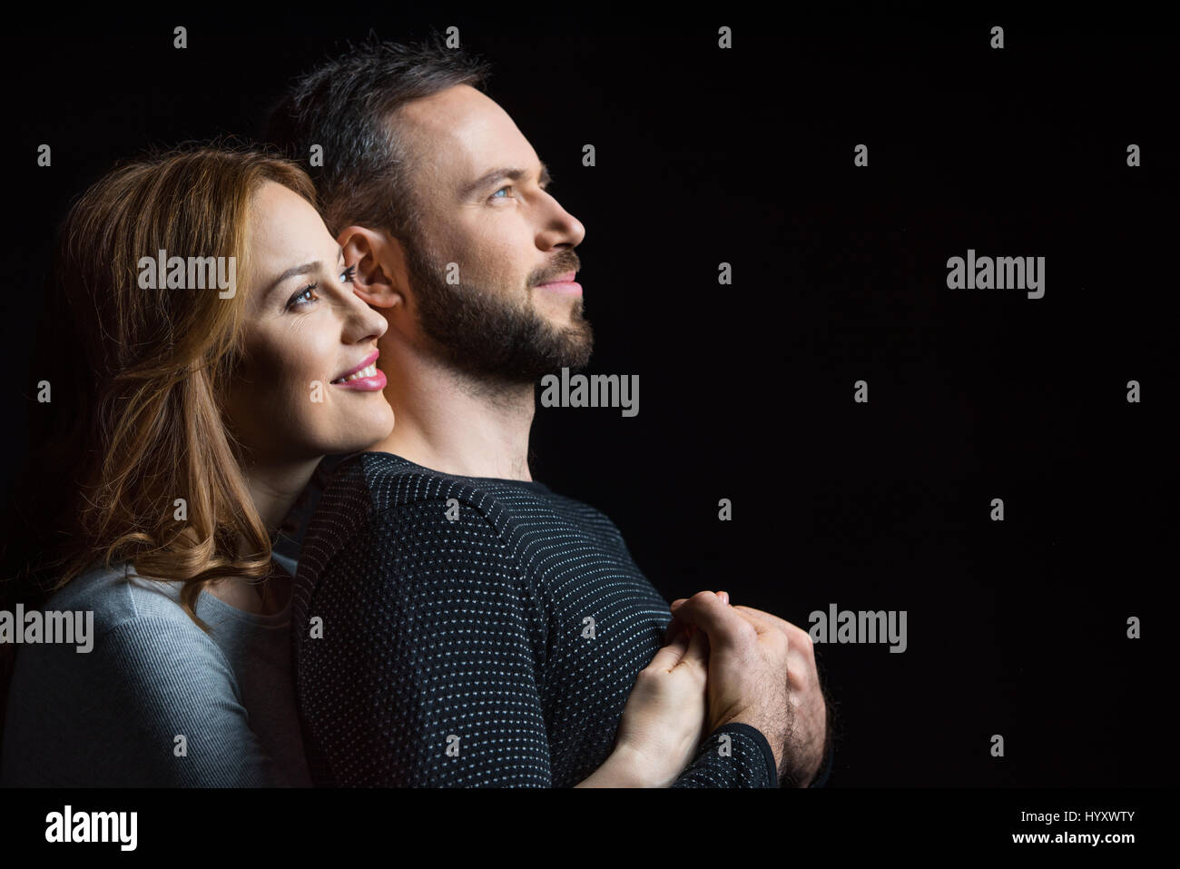 Side view of smiling young woman hugging her boyfriend from behind on ...