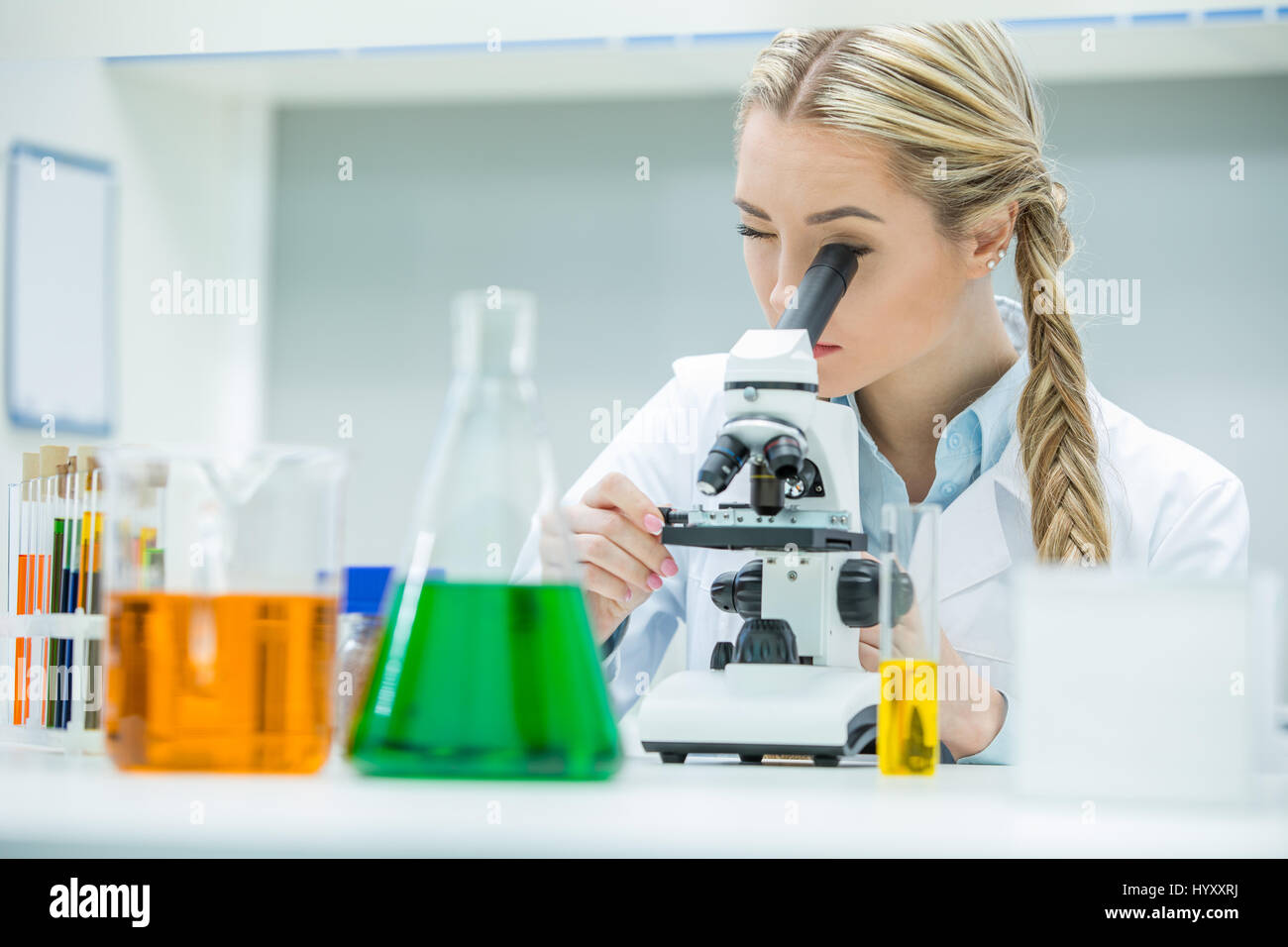 Young female scientist working with microscope in chemical laboratory ...