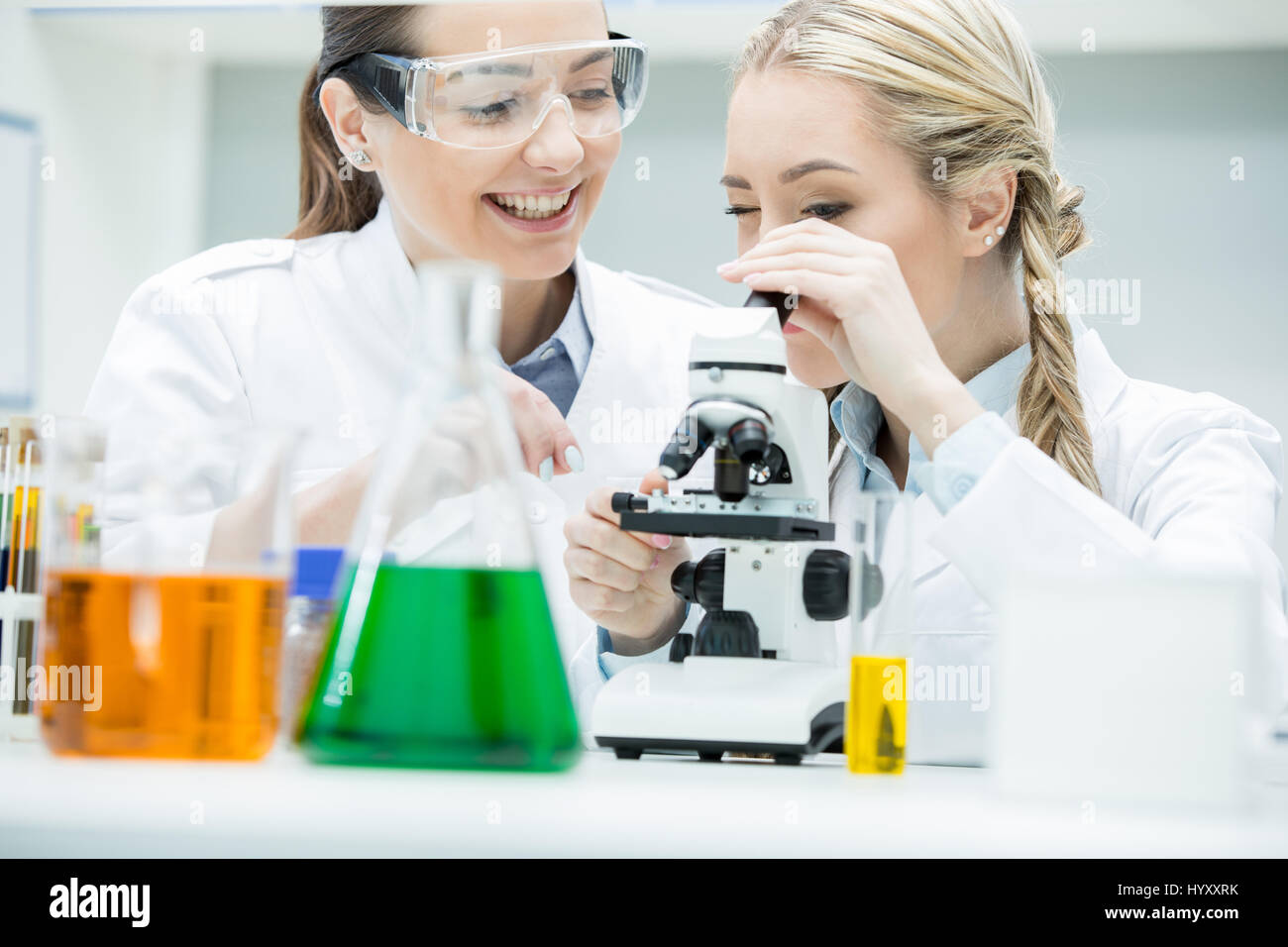 Smiling female scientists working with microscope in chemical ...