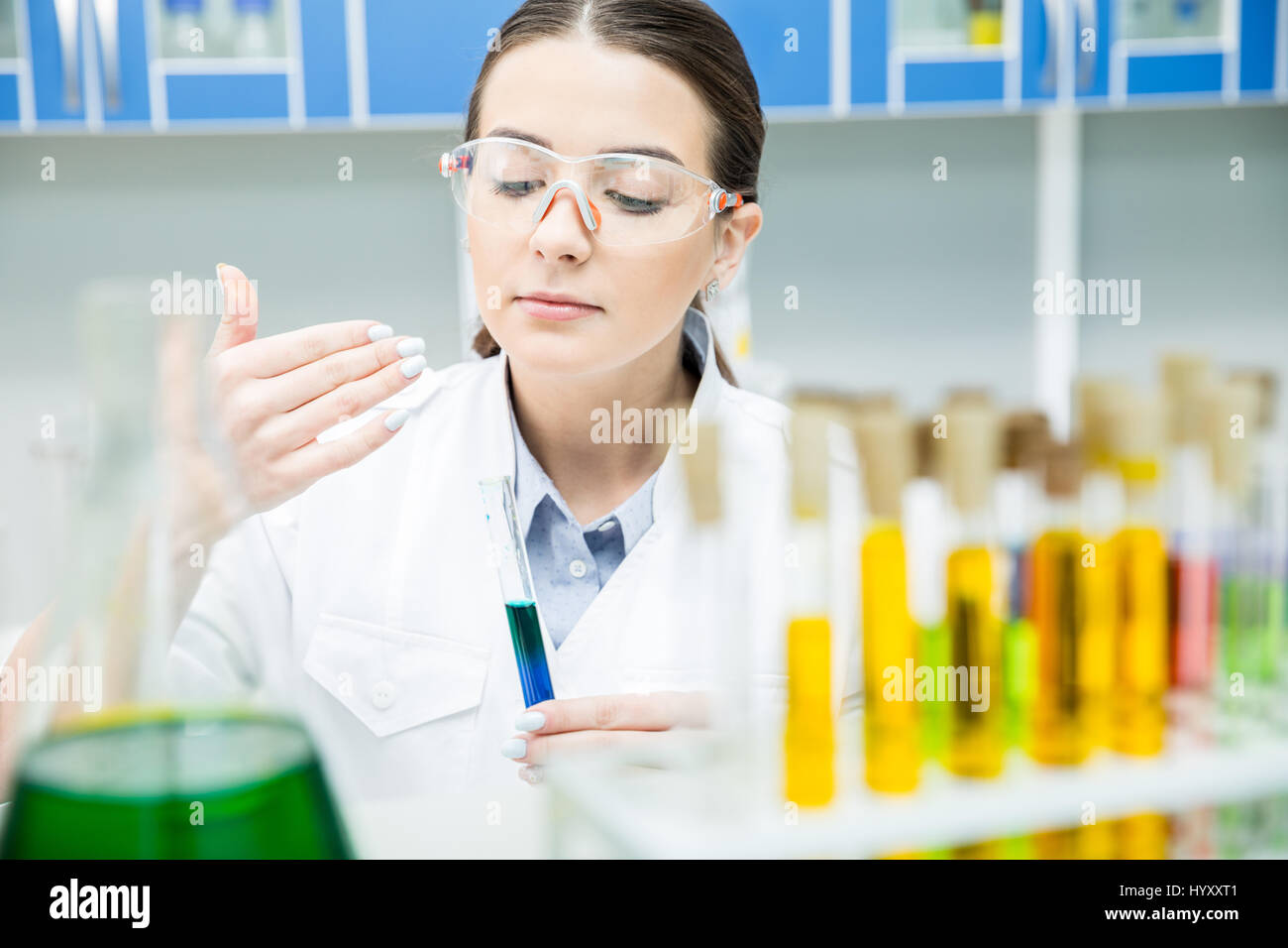 Young female scientist examining chemical sample in test tube in lab ...