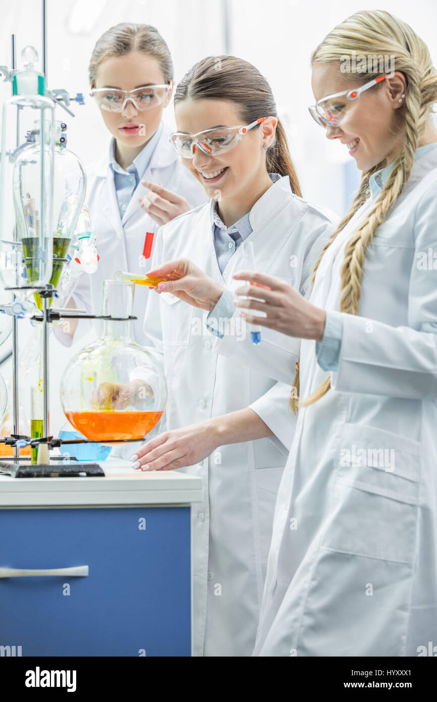 Three young smiling female scientists making experiment in chemical lab ...