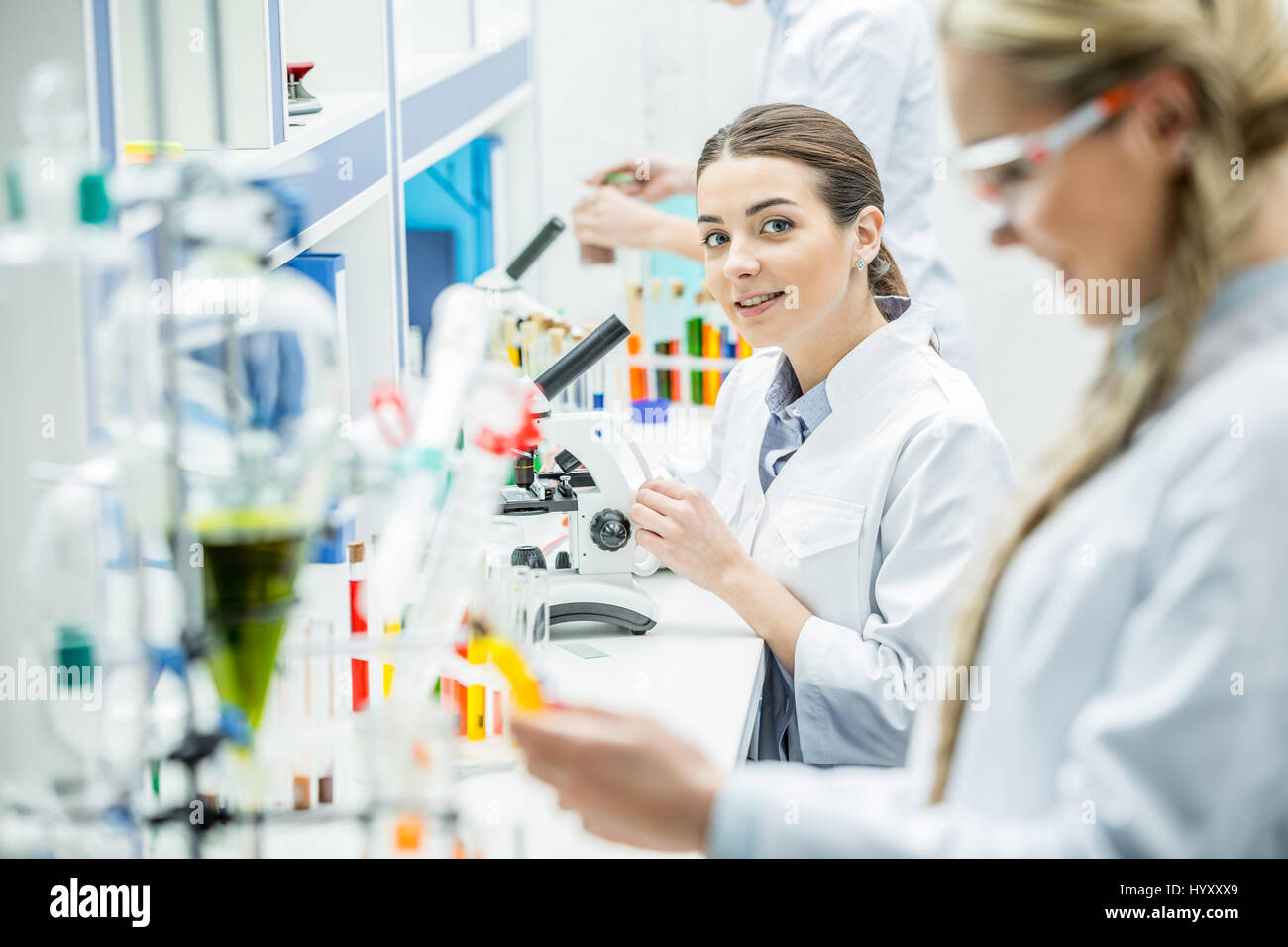 Young female scientist working with microscope and looking at camera in ...