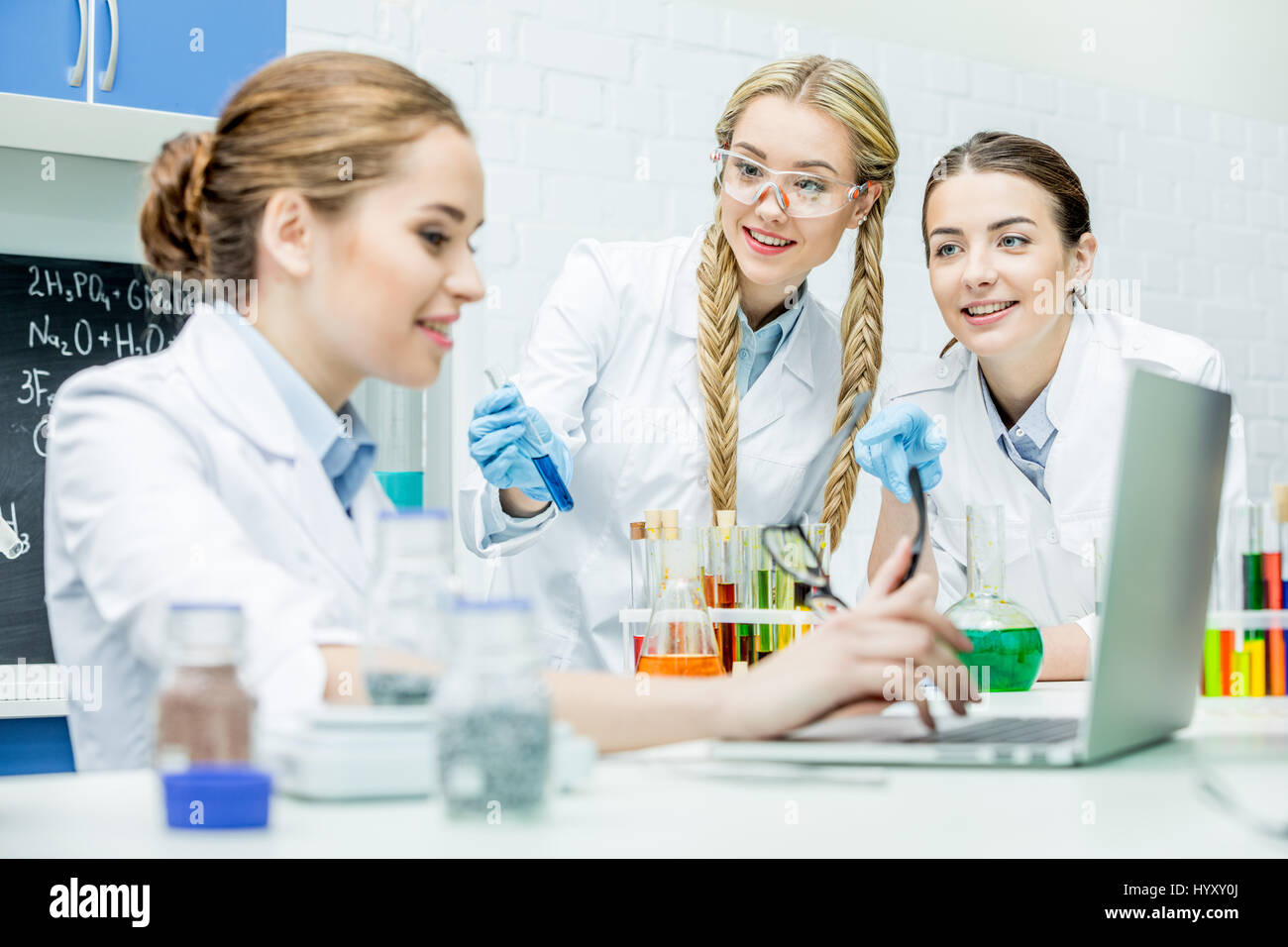 Female scientists working with laptop and reagents in chemical ...