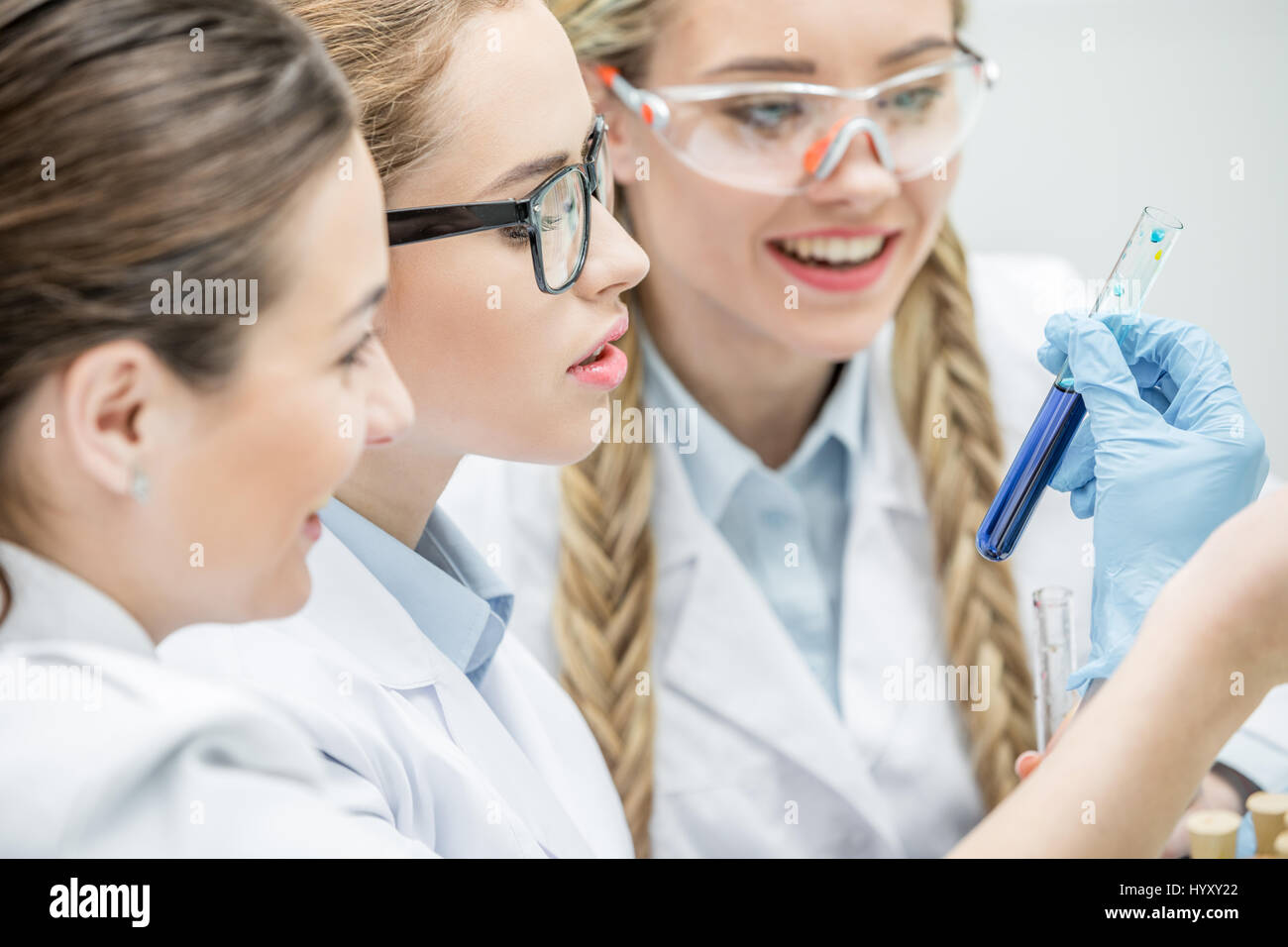 Young female scientists examining chemical sample in test tube in ...