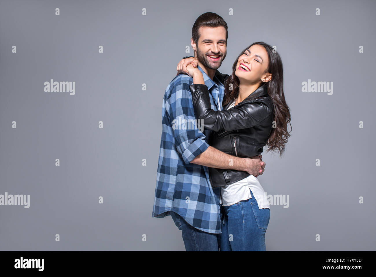 Happy young couple hugging and looking at camera on grey Stock Photo ...