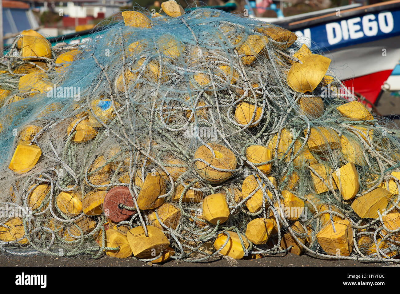 Fishing nets piled on the beach next to a colourful fishing boat in the ...