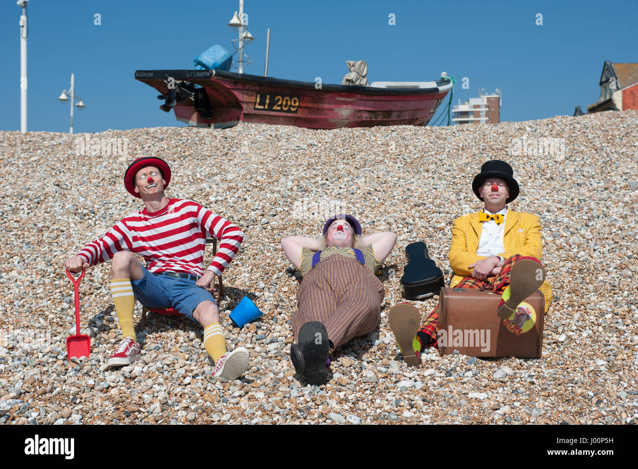 Three clowns sitting on the beach sunbathing on a sunny day during the ...