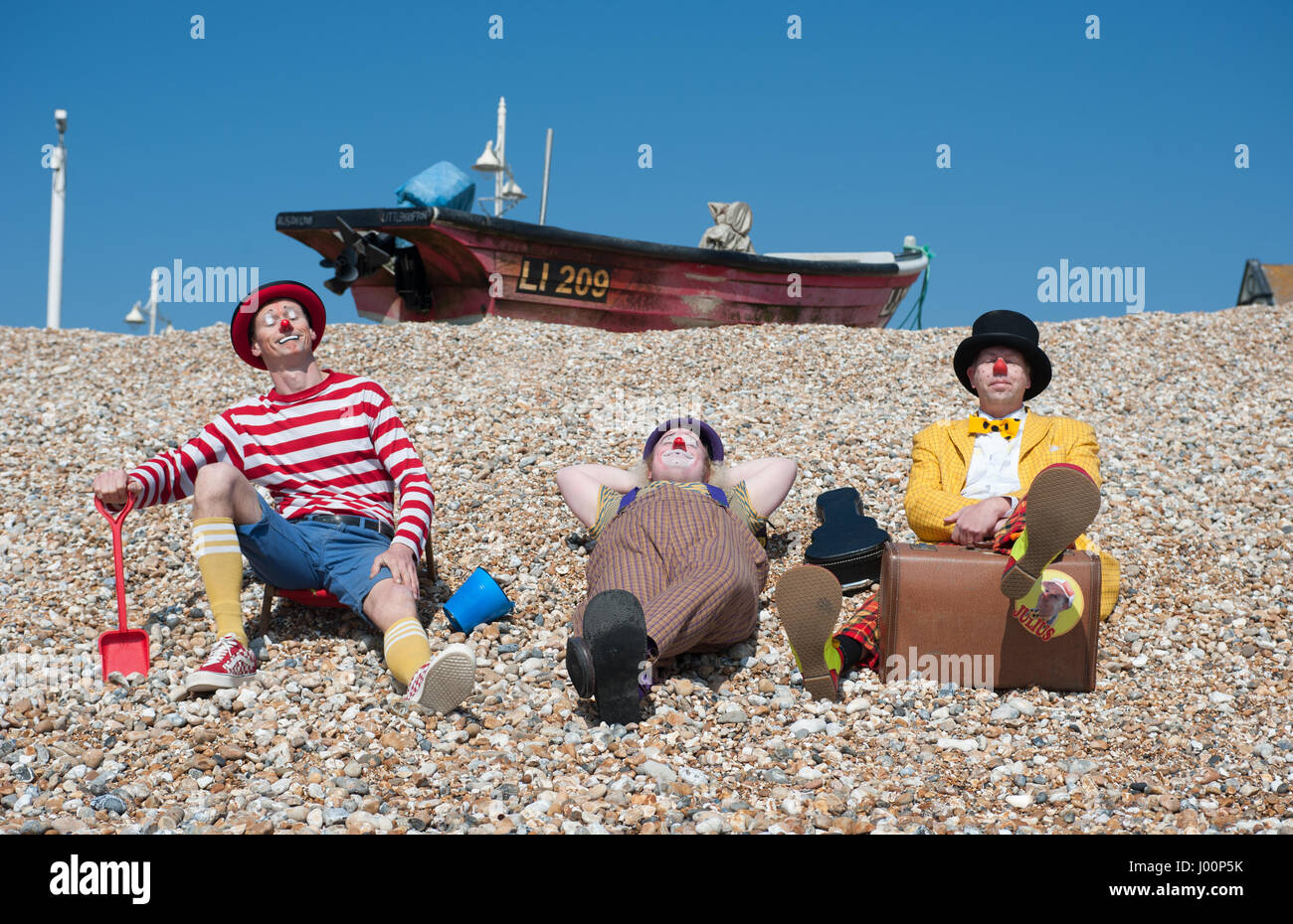 Three clowns sitting on the beach sunbathing on a sunny day during the ...