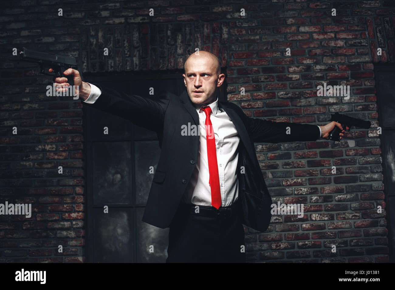 Serious hired assasin in red tie aims with two pistols. Professional ...