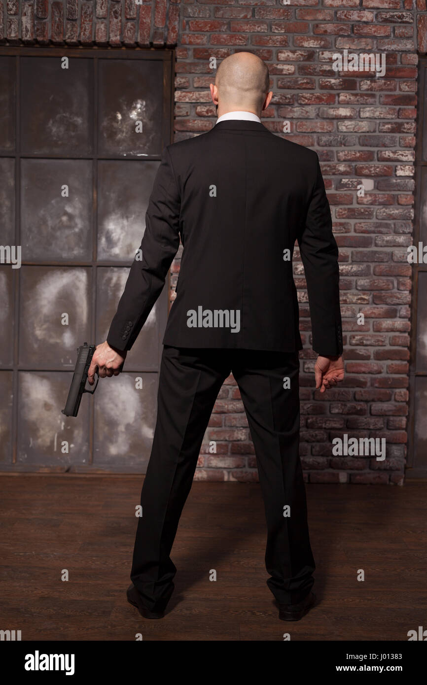 Contract murderer with gun wallpaper concept, back view. Bald assassin ...