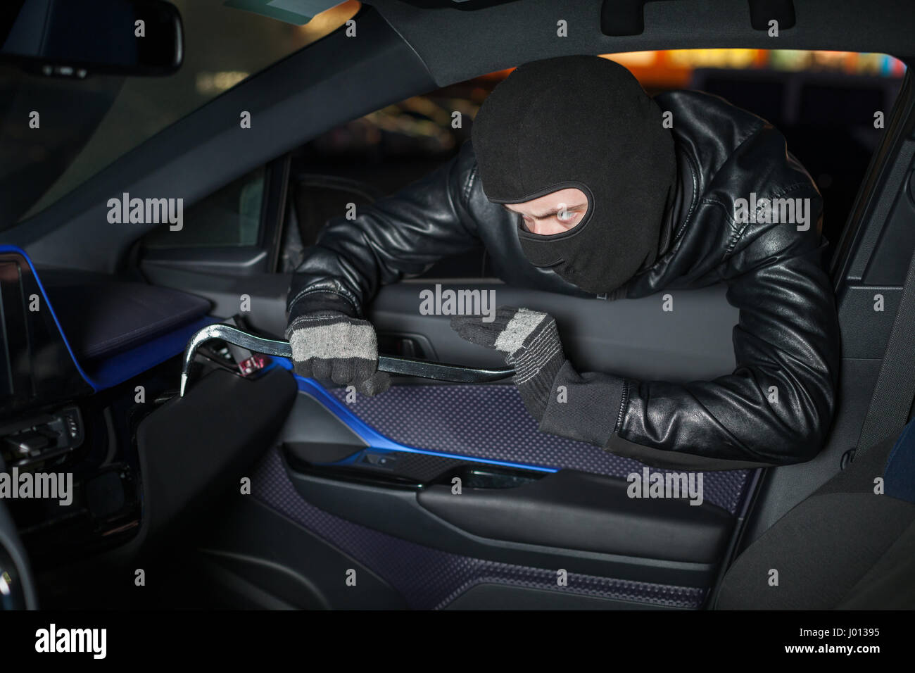 Carjacker unlock glove box with crowbar. Male thief with balaclava on ...