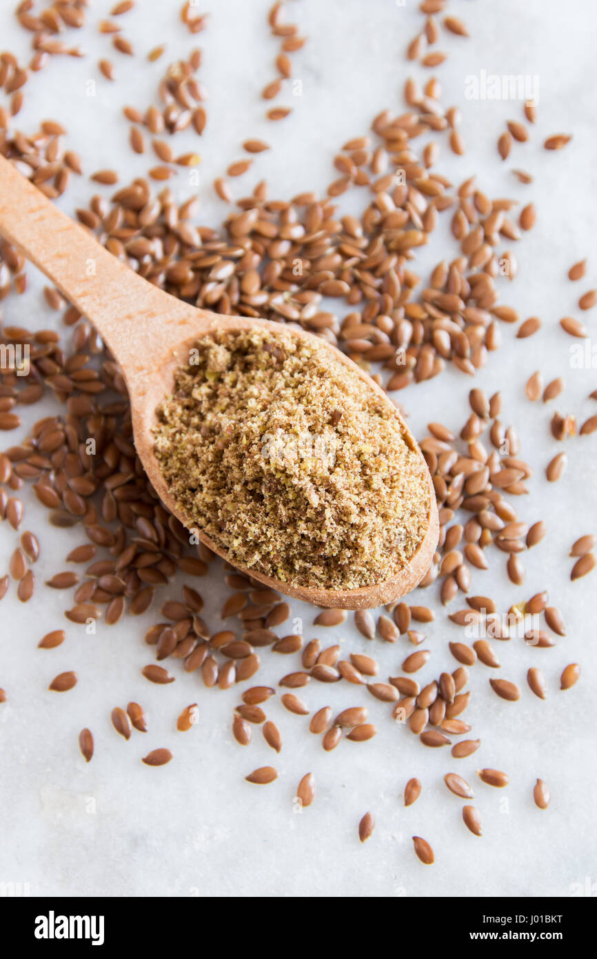 Crushed flax seeds (ground linseed) on wooden spoon and white stone table - healthy organic ...