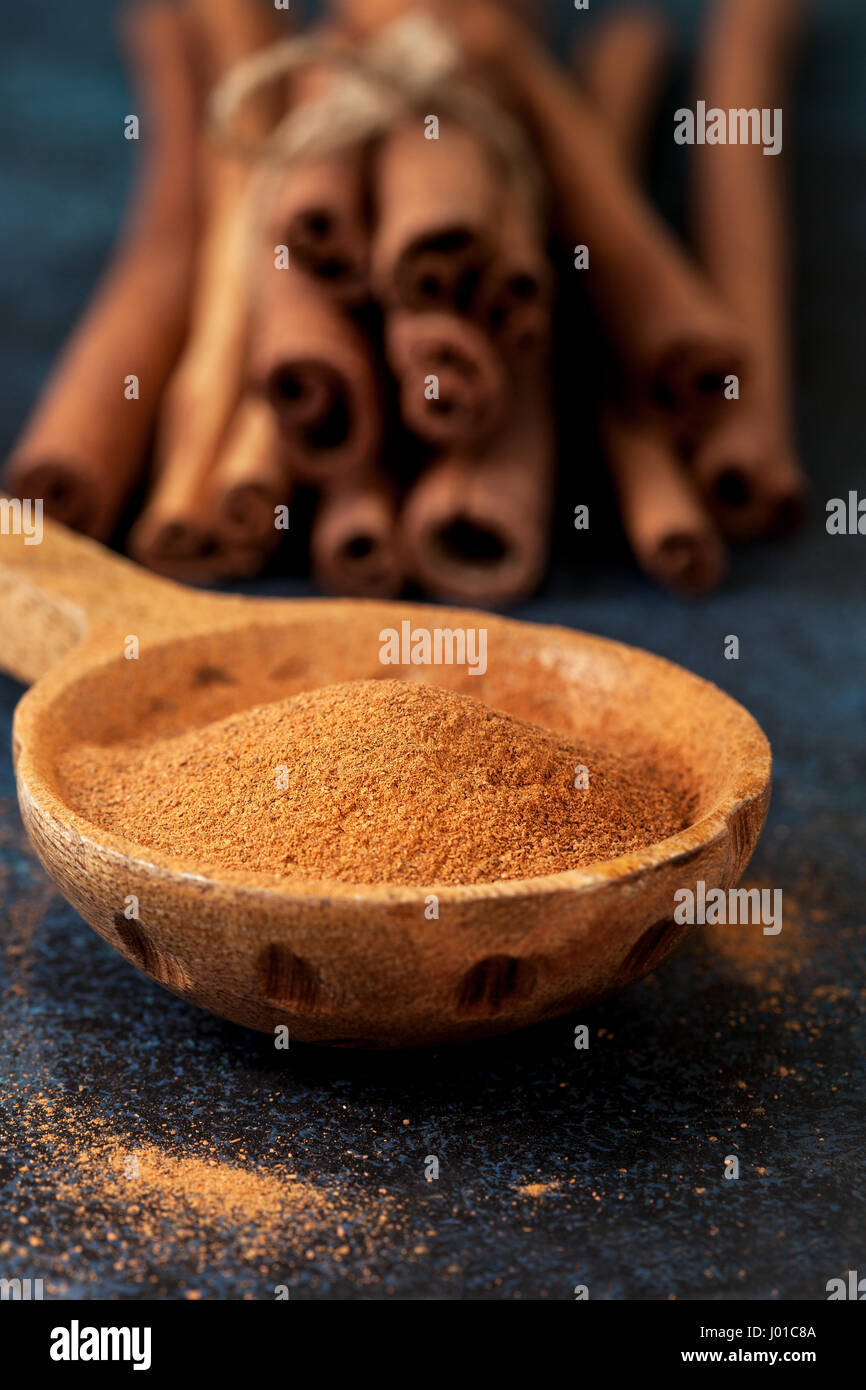 Ground cinnamon in a wooden spoon, cinnamon sticks on blue background ...