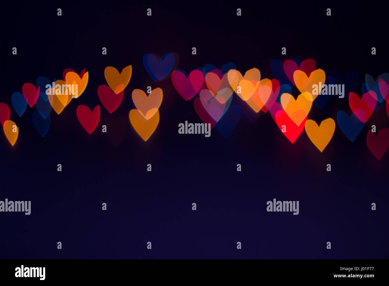 Line of colorful blurred heart shape lights on dark blue background ...