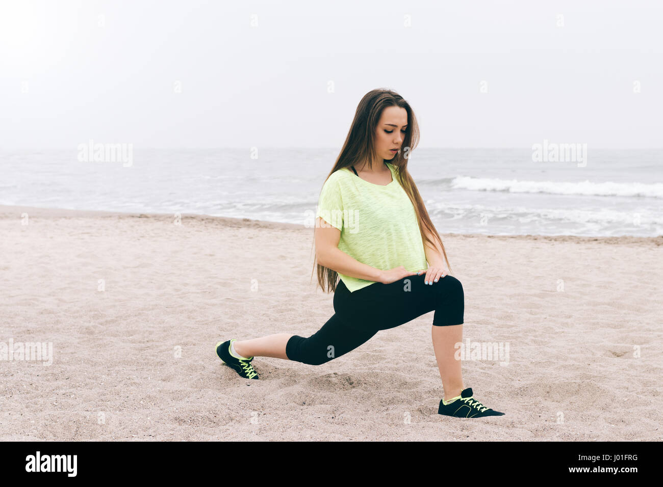Sporty slender girl doing stretching on the beach on a cloudy day, wide ...