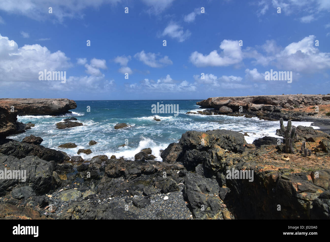 Rugged lava rocks encircling the cove of Aruba's black sand stone beach ...