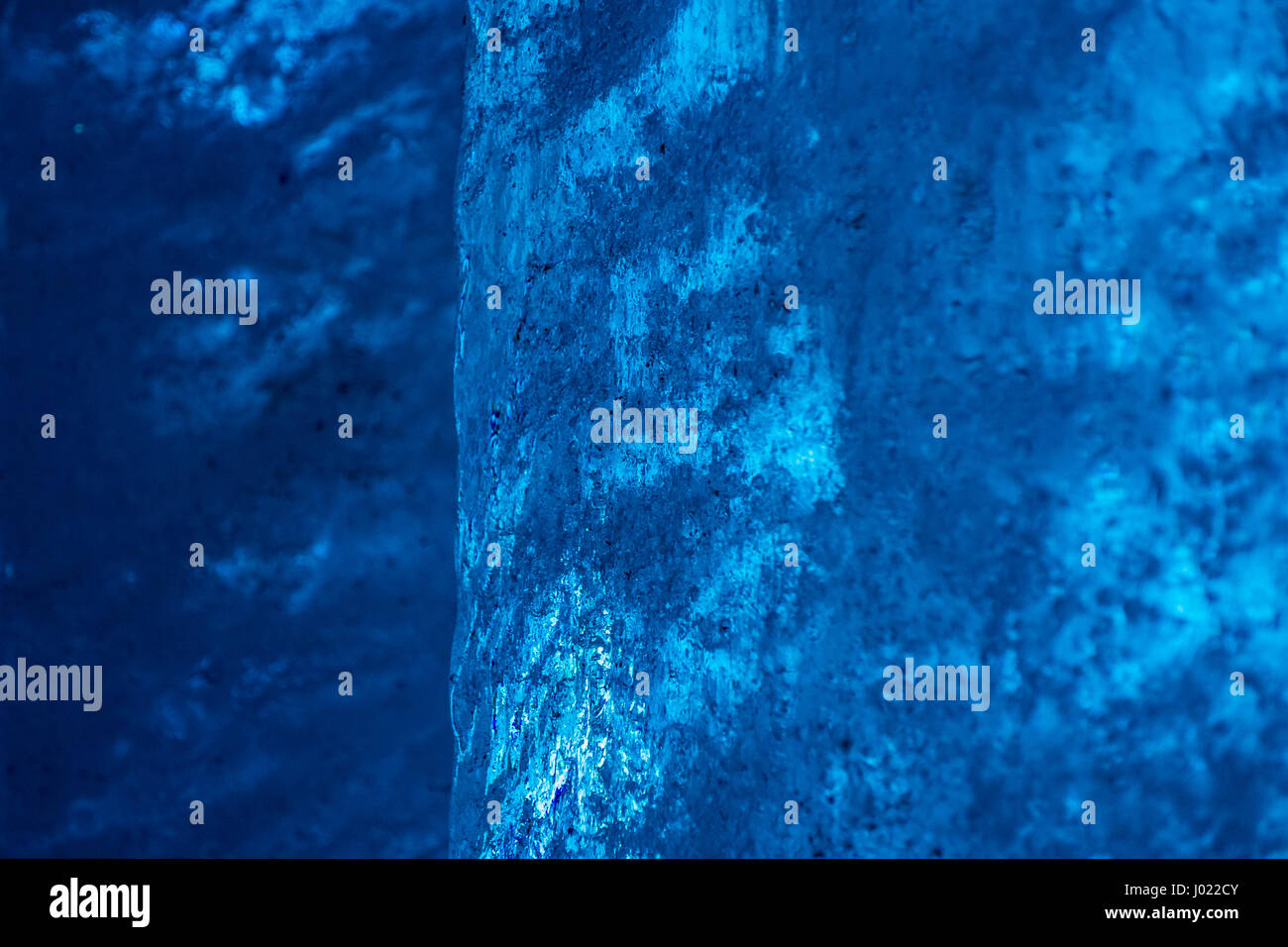 Detail of blue ice wall inside glacier tunnel illuminated by sunlight ...