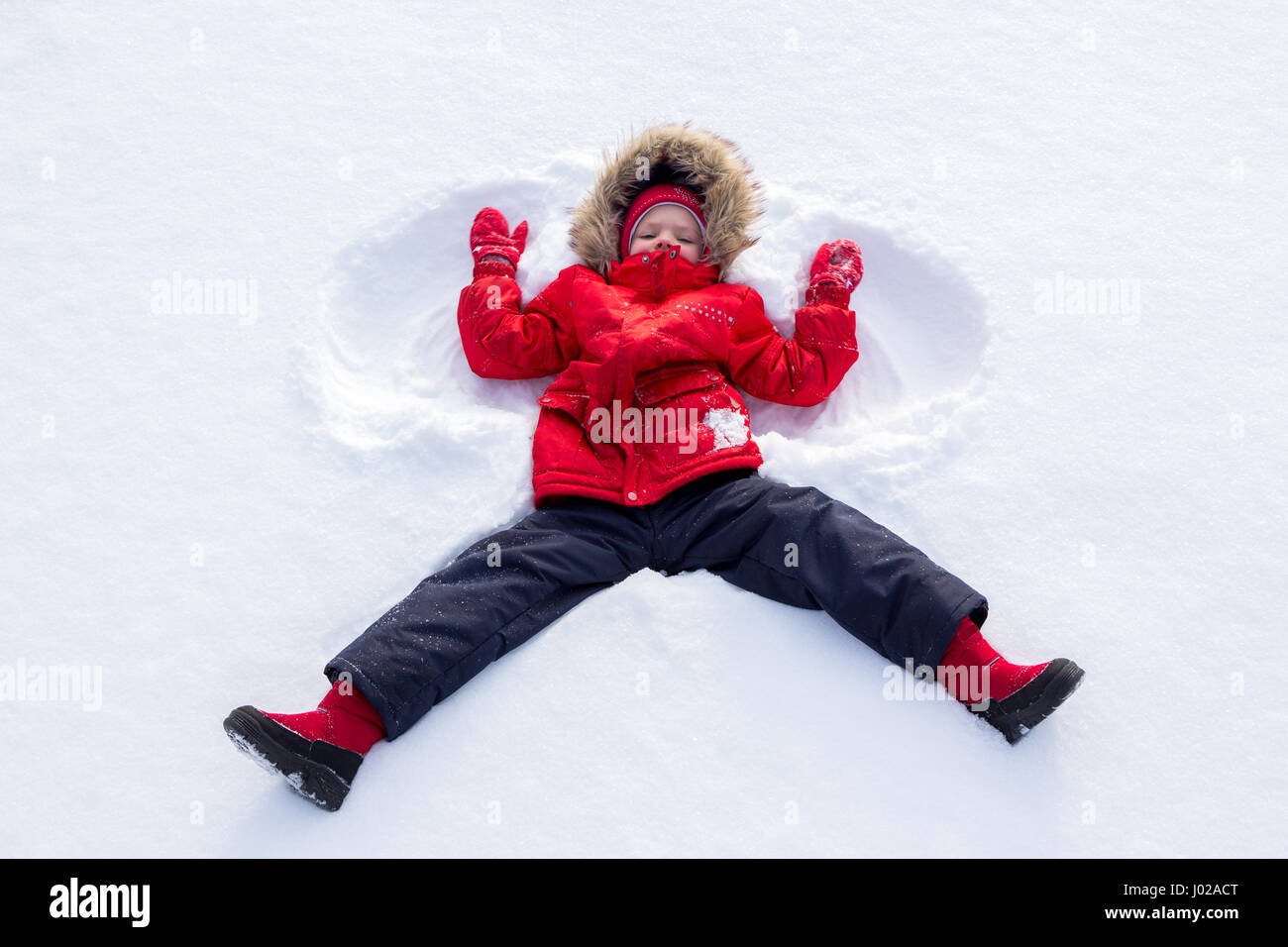 Girl in a red jacket makes a snow angel Stock Photo - Alamy