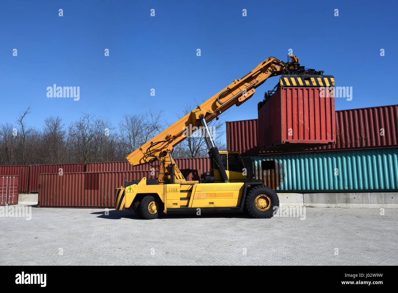 Yellow container handling vehicle in action lifting up red metal ...