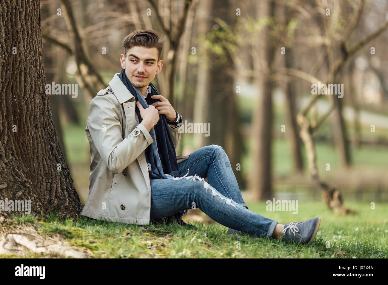 Fashionable man sitting near trees with blur background Stock Photo - Alamy