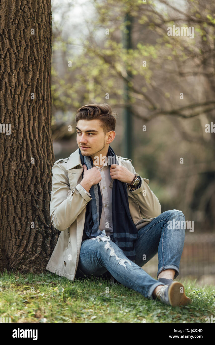 Fashionable man sitting near trees with blur background Stock Photo - Alamy
