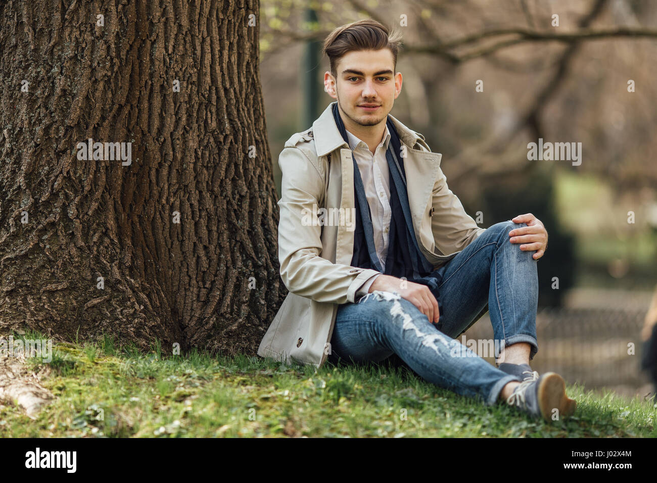 Fashionable man sitting near trees with blur background Stock Photo - Alamy