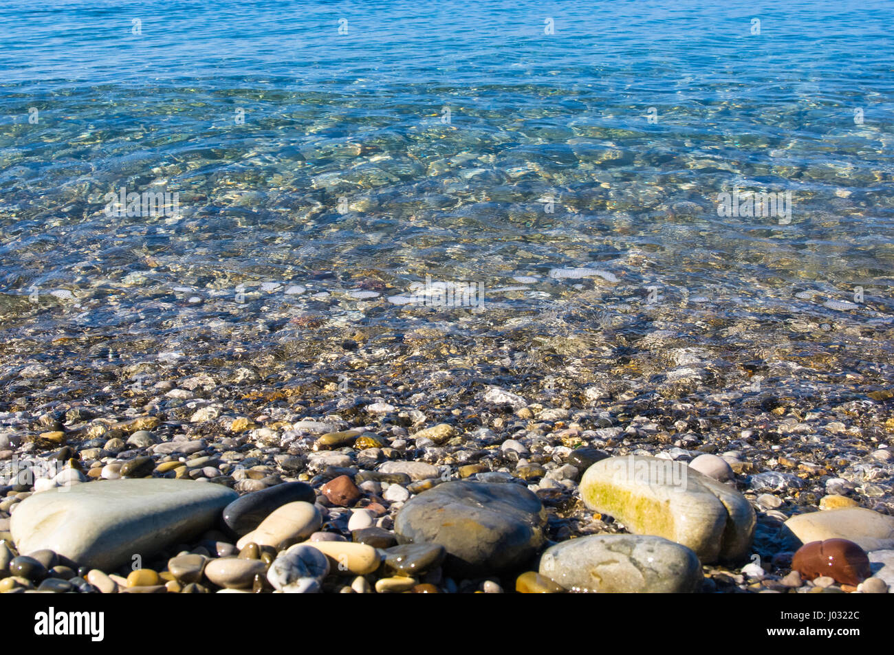 sea pebble beach with multicoloured stones, transparent waves with foam ...
