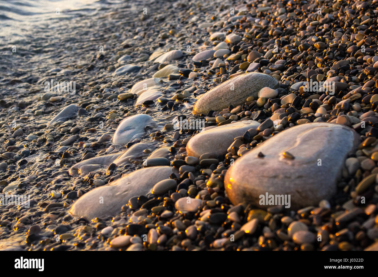 sea pebble beach with multicoloured stones, transparent waves with foam ...